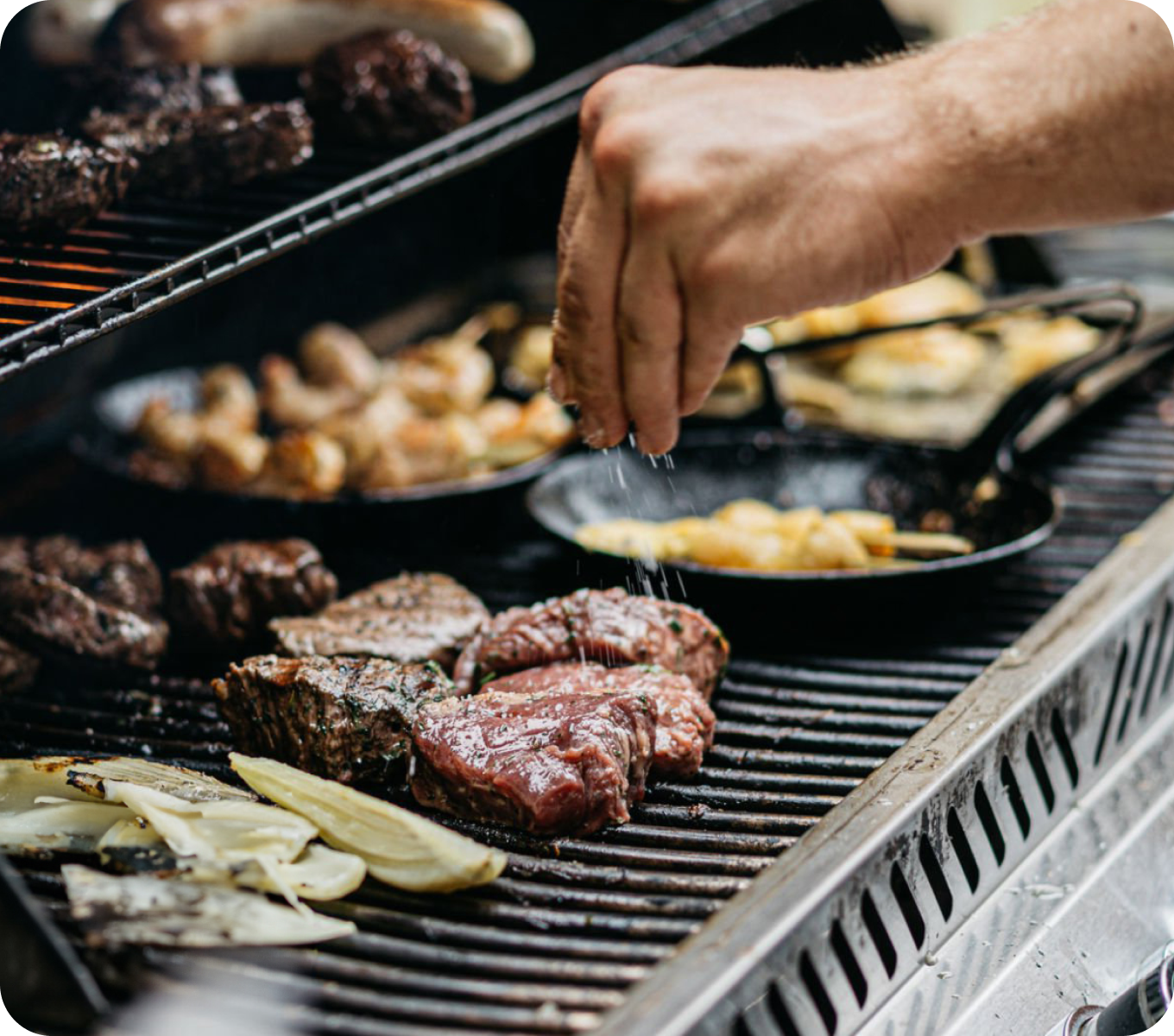 A hand sprinking salt over meat on a barbecue grill